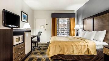Quarto de hotel com cama, escrivaninha, televisão, frigorífico e janela com cortinas.