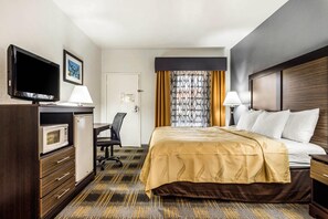 Quarto de hotel com cama, escrivaninha, televisão, frigorífico e janela com cortinas.