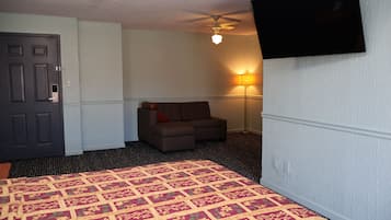 Quarto de hotel com cama, sofá, televisão fixada na parede, ventoinha de teto e luminária na parede.
