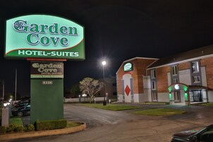 Placa de identificação do Garden Cove Hotel-Suites, com vista clara da entrada do edifício e estacionamento.