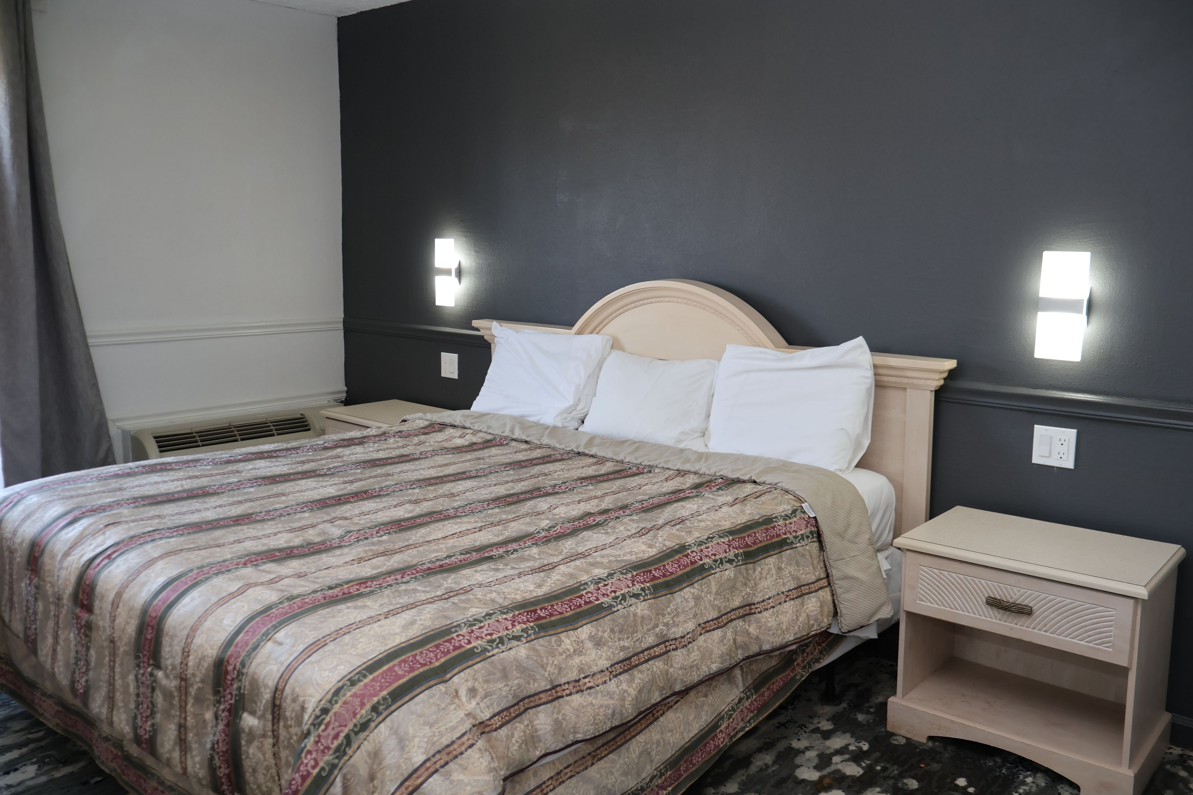 Quarto de hotel com cama, mesas de cabeceira e luminária fixada na parede.