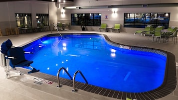 Piscina interna com superfície de água cristalina, rodeada por espreguiçadeiras e uma área de estar com mesas.