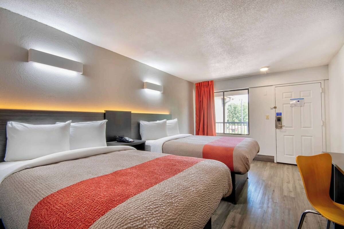 Quarto de hotel com duas camas, uma escrivaninha e uma cadeira.