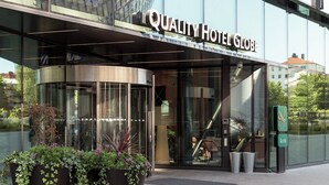 Uma entrada de hotel moderna com porta giratória, grandes janelas de vidro e plantas em vasos.