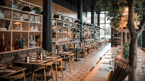 Restaurante com várias mesas e cadeiras, prateleiras com objetos decorativos e uma grande árvore no centro.