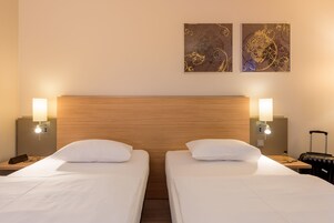 Quarto de hotel com duas camas de solteiro, cabeceira de madeira, abajures e duas obras de arte penduradas na parede.