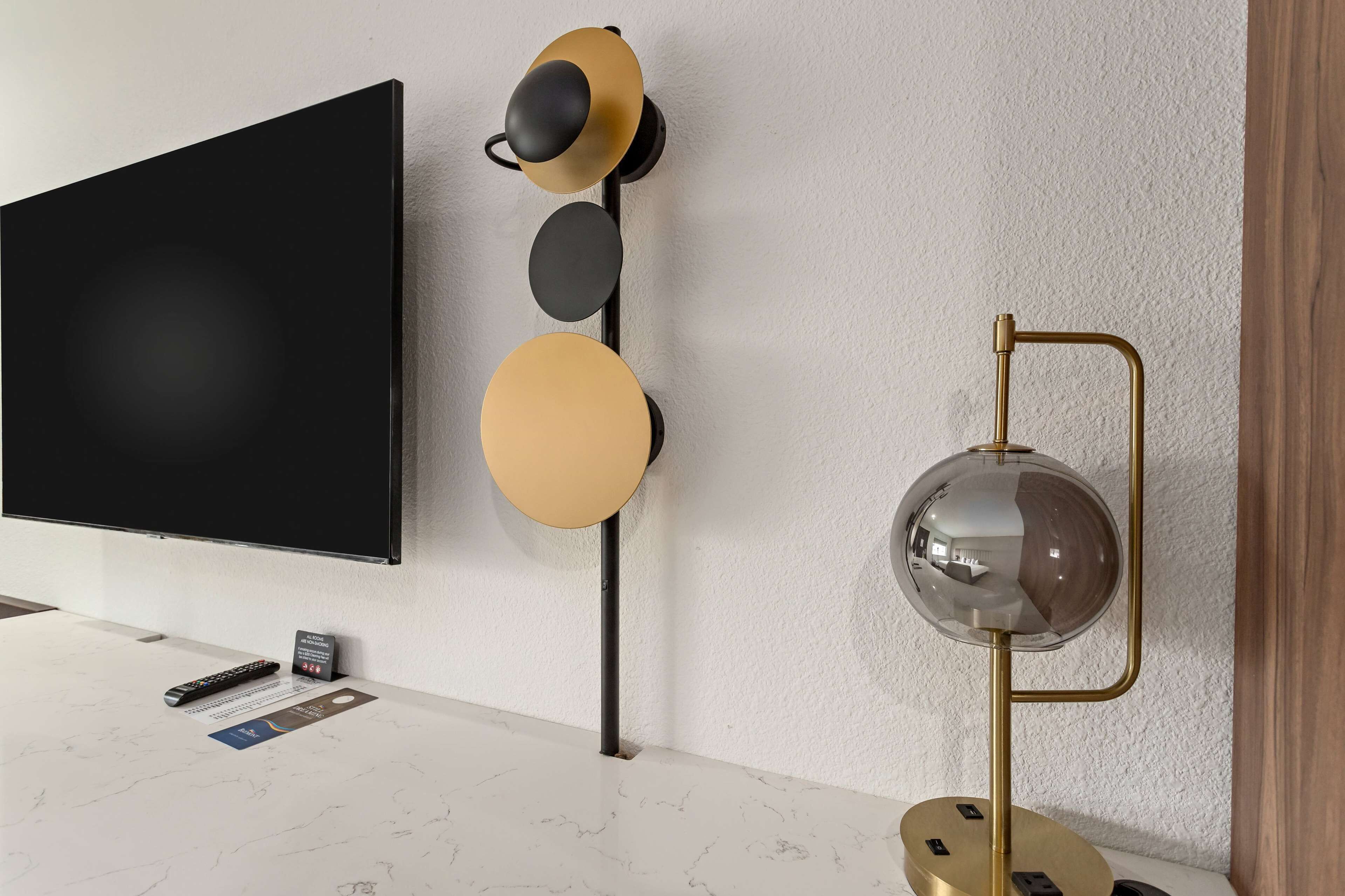 Quarto de hotel moderno com uma televisão de tela plana grande fixada na parede, uma luminária esférica única e decoração minimalista.