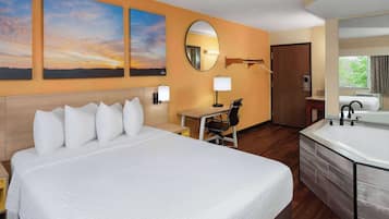 Quarto de hotel com uma cama grande, uma escrivaninha, uma cadeira, banheiro com banheira e duas pinturas do pôr do sol na parede.