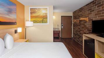 Quarto de hotel com uma cama, televisão, parede de tijolos e uma pintura do pôr do sol.