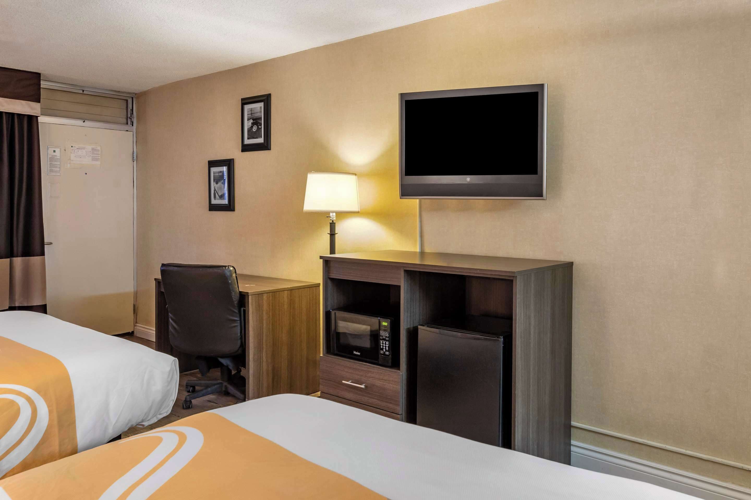Quarto de hotel com duas camas, uma escrivaninha com micro-ondas, frigorífico, televisão e uma lâmpada.