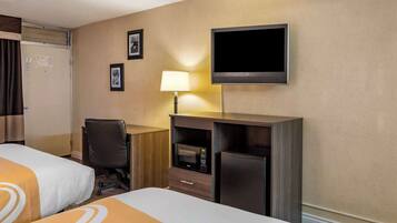 Quarto de hotel com duas camas, uma escrivaninha com micro-ondas, frigorífico, televisão e uma lâmpada.