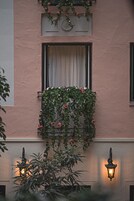 Fachada de edifício com uma janela decorada por rosas trepadeiras e um candeeiro fixado na parede.