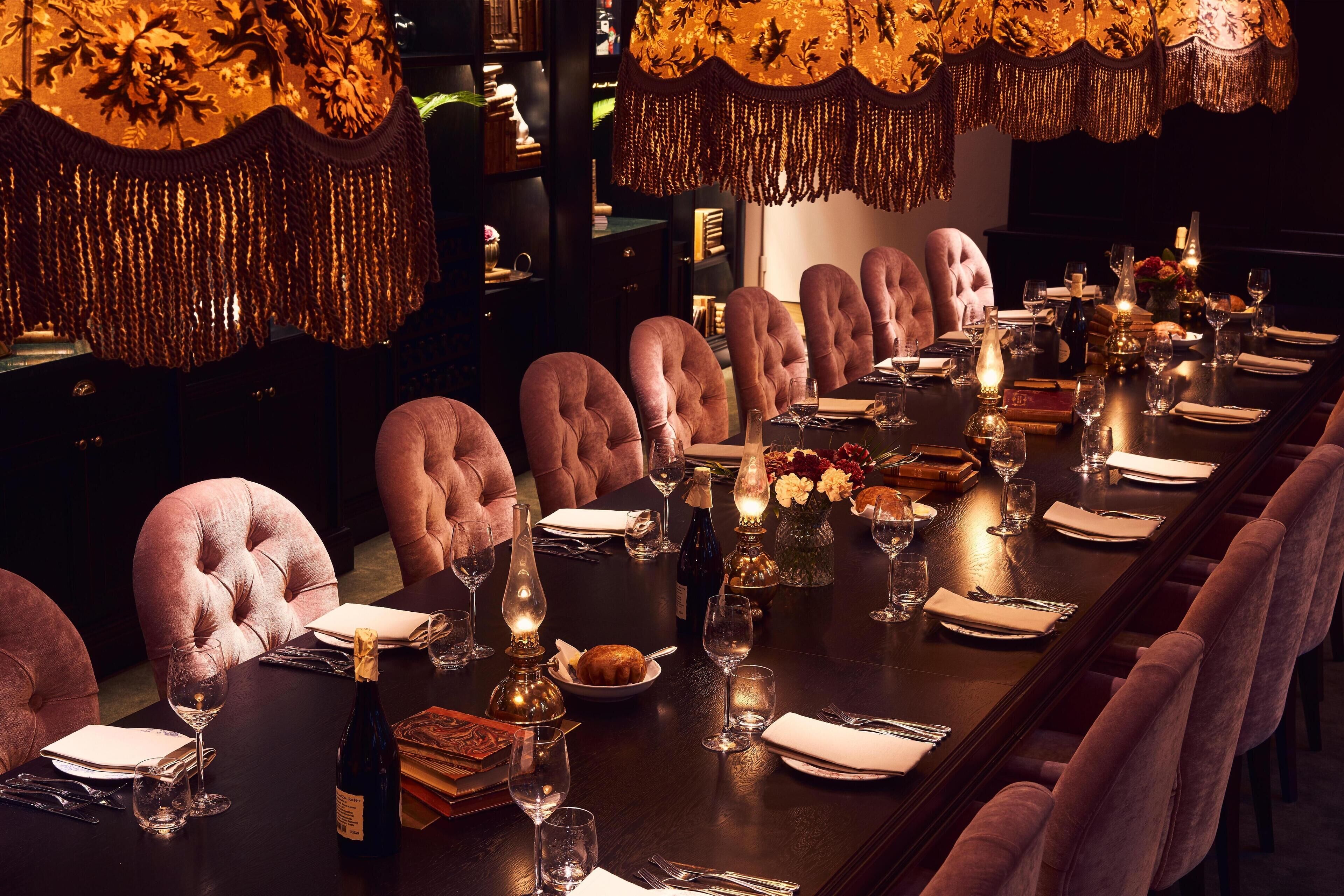 Uma sala de jantar formal com uma mesa comprida, cadeiras luxuosas e elegantes louças, incluindo copos de vinho, pratos e uma garrafa de vinho.