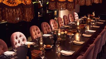 Uma sala de jantar formal com uma mesa comprida, cadeiras luxuosas e elegantes louças, incluindo copos de vinho, pratos e uma garrafa de vinho.