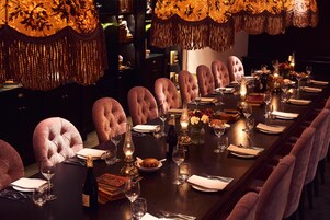 Uma sala de jantar formal com uma mesa comprida, cadeiras luxuosas e elegantes louças, incluindo copos de vinho, pratos e uma garrafa de vinho.