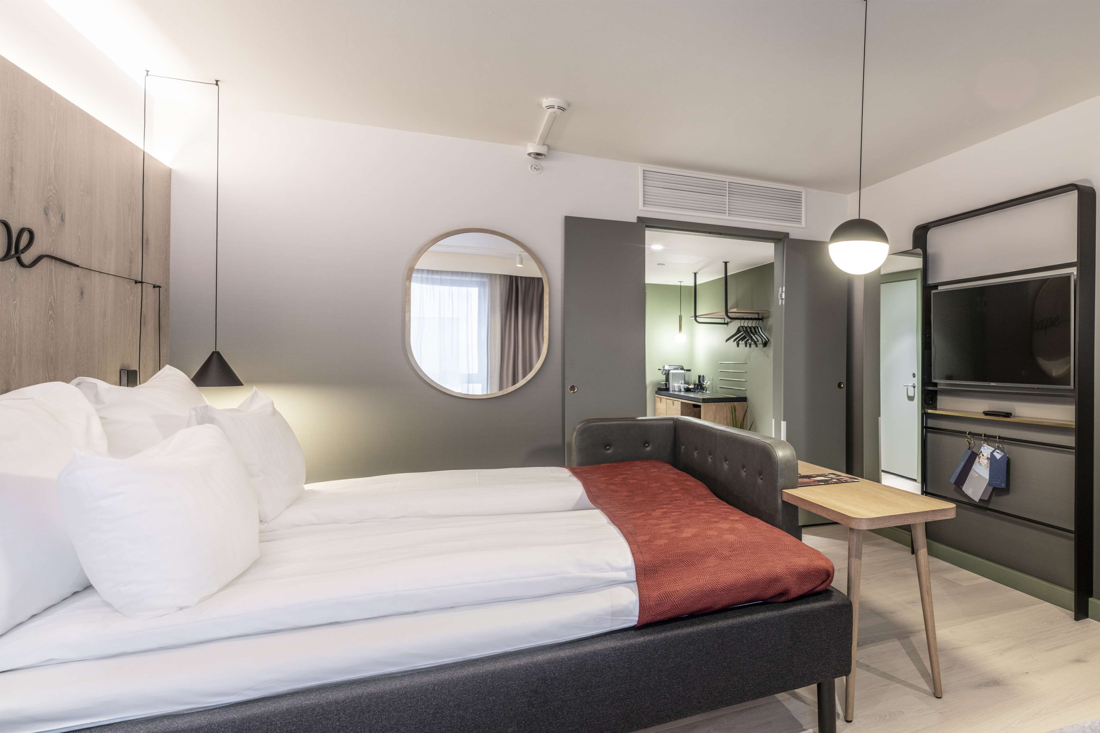 Quarto de hotel moderno com cama, escrivaninha, espelho e televisão.
