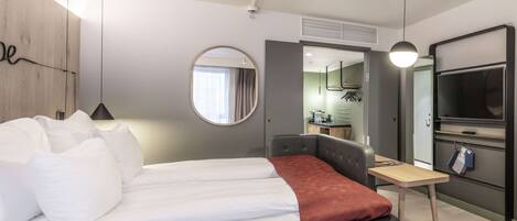 Quarto de hotel moderno com cama, escrivaninha, espelho e televisão.