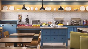 Uma cozinha moderna com armários azuis, uma ilha central com micro-ondas, torradeira e máquina de café, e uma área de jantar com mesas e cadeiras de madeira.