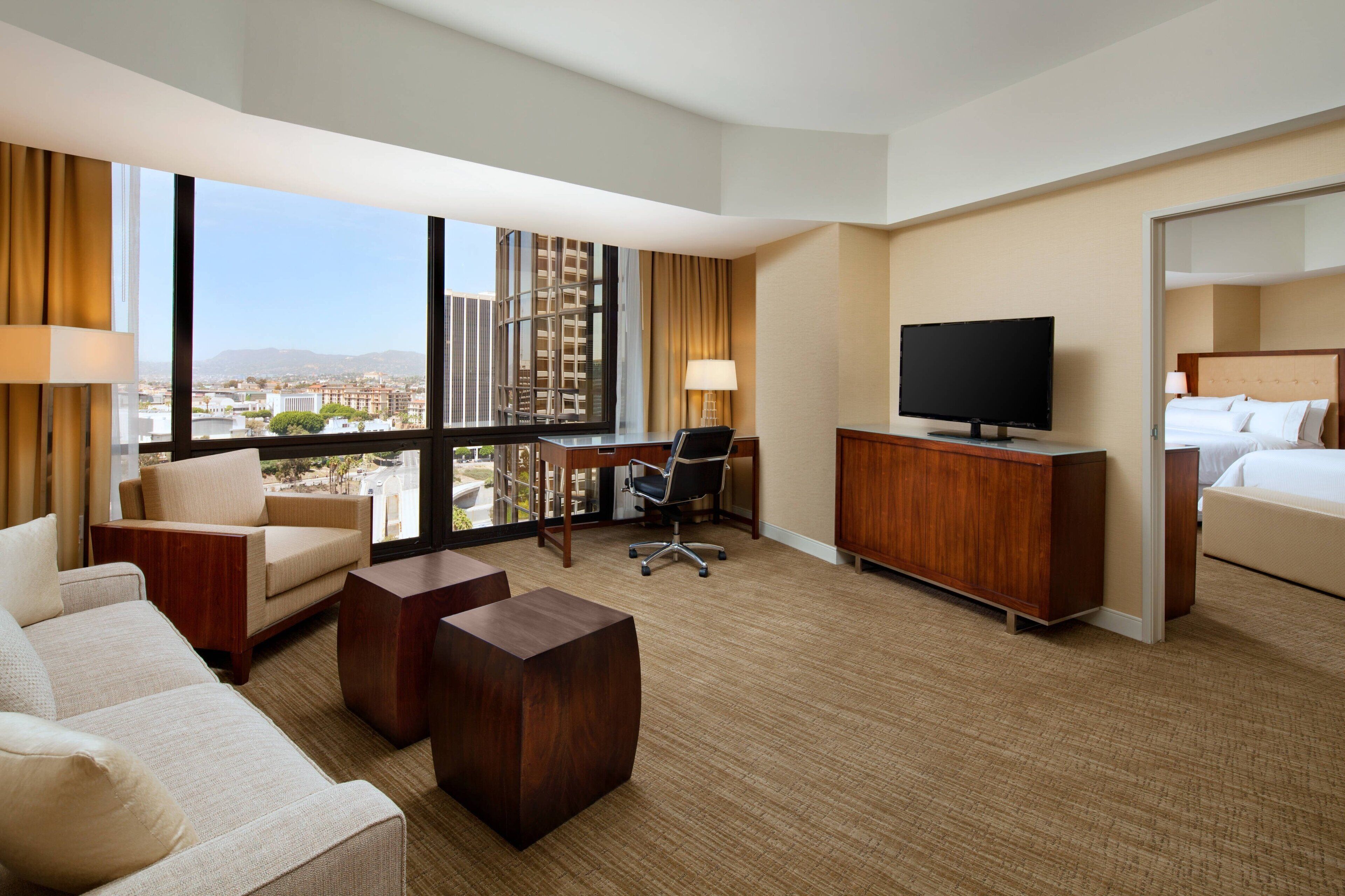 Quarto de hotel com uma janela grande, televisão, escrivaninha, cama e sofá.