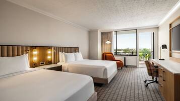 Quarto de hotel com duas camas, uma mesa, uma cadeira e uma janela grande com vista.