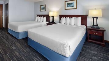 Quarto de hotel com duas camas, cabeceira de madeira, mesa de cabeceira com abajur e quadro na parede.
