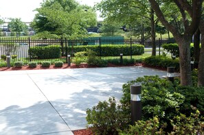 Uma passarela pavimentada com cerca de metal e vegetação, que leva a um edifício com telhado verde.