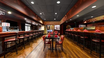 Um restaurante com soalho de madeira, cadeiras vermelhas e uma mesa de jantar central.