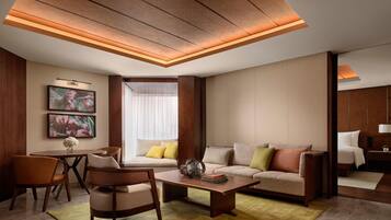 Quarto de hotel moderno com sofá, poltronas, mesa de centro e televisão.