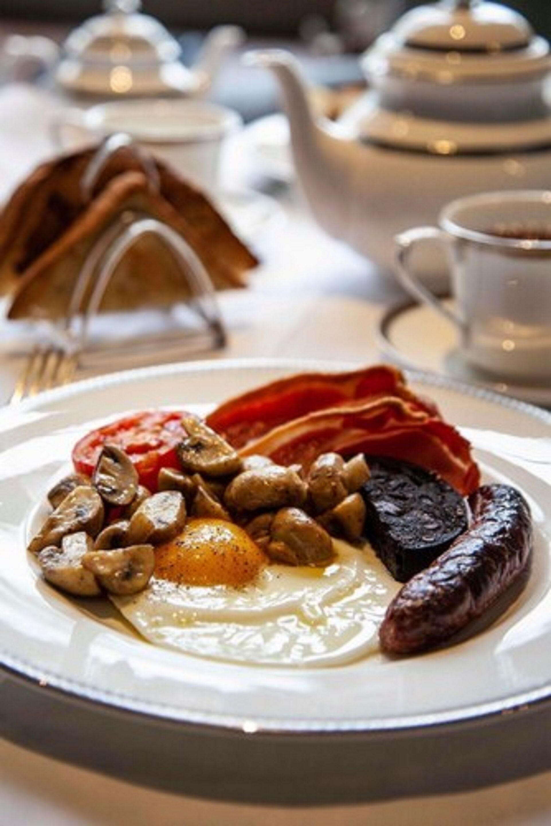Prato de café da manhã com ovos, cogumelos, bacon, linguiça e fatias de tomate.