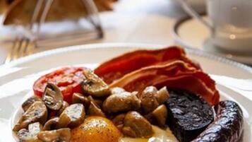 Prato de café da manhã com ovos, cogumelos, bacon, linguiça e fatias de tomate.