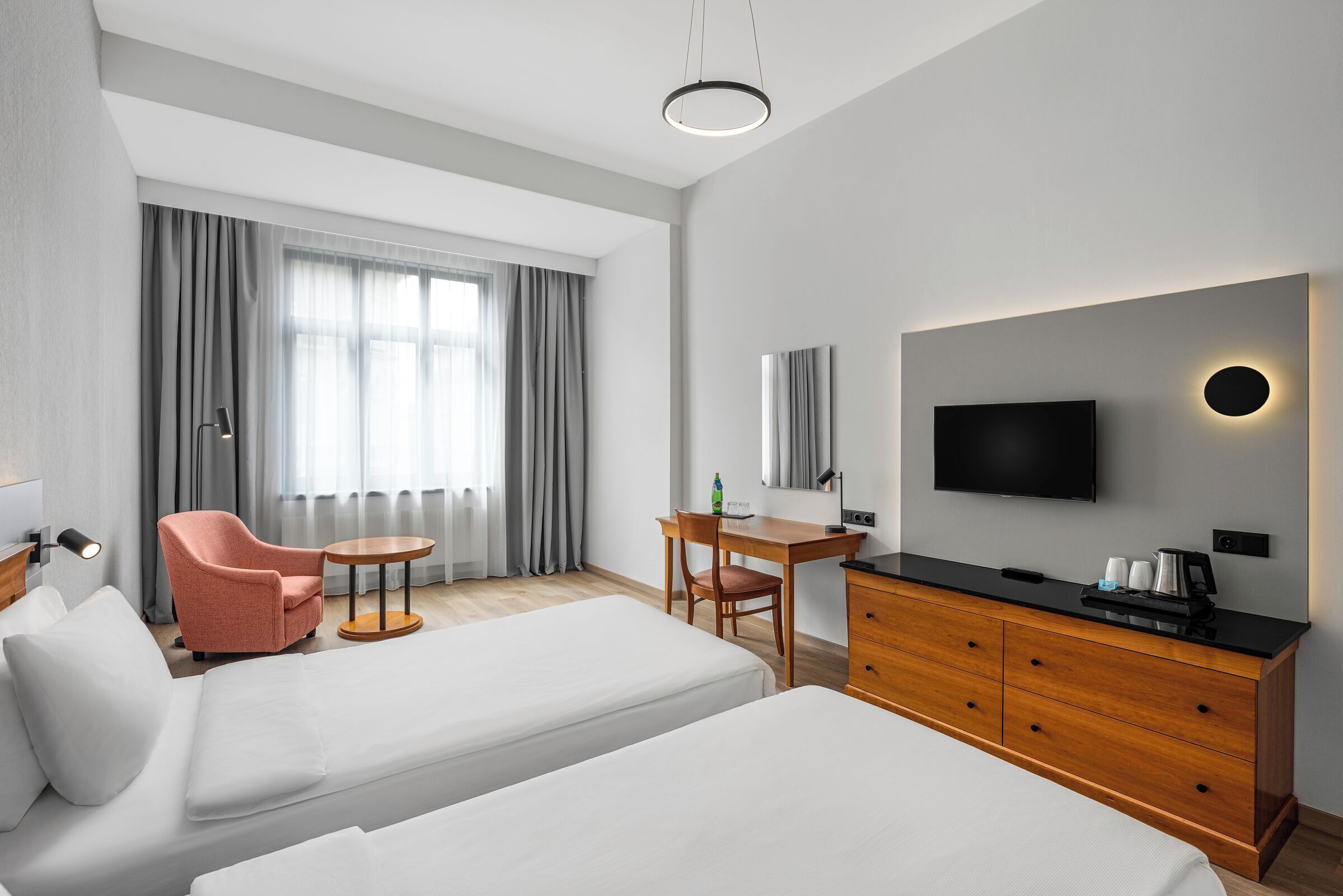 Quarto de hotel com duas camas, uma escrivaninha, uma cadeira, uma televisão e um minibar.