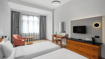 Quarto de hotel com duas camas, uma escrivaninha, uma cadeira, uma televisão e um minibar.
