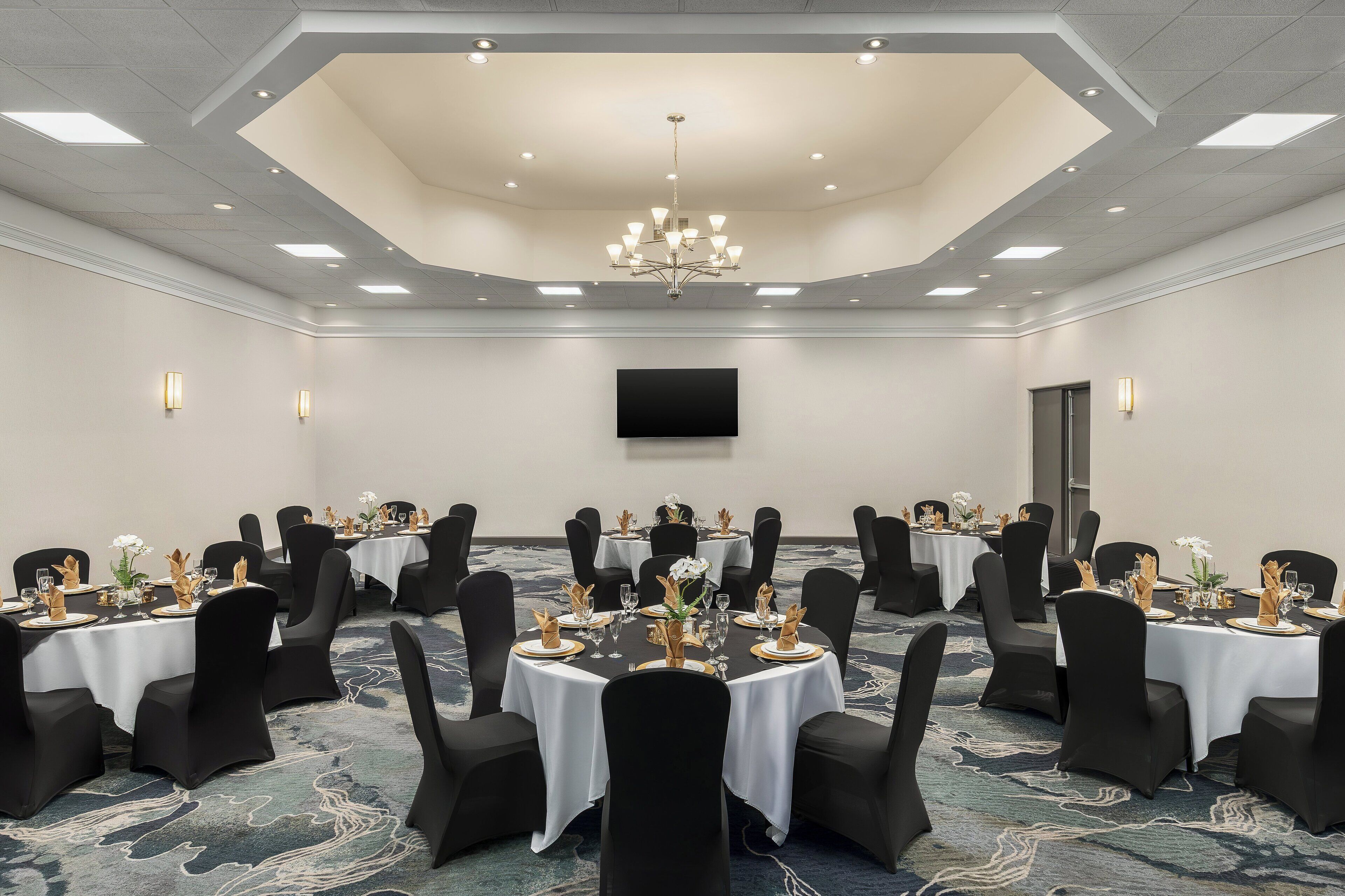 Uma sala de conferências com mesas redondas, cadeiras pretas e um lustre.