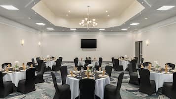 Uma sala de conferências com mesas redondas, cadeiras pretas e um lustre.