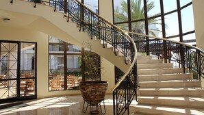 Uma escadaria imponente com design curvo, que conduz a um andar superior. Um grande vaso com planta está posicionado na base da escada.