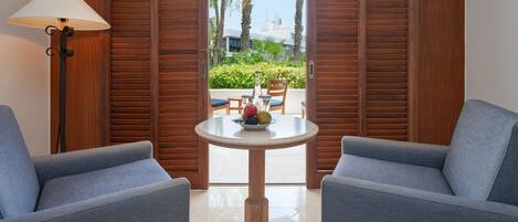 Um quarto com uma mesa redonda, duas poltronas azuis, um abajur e persianas de madeira.