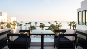 Varanda com mesa e cadeiras, vista para uma piscina e o oceano.