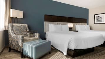 Quarto de hotel com uma cama grande, uma cadeira, uma escrivaninha e um abajur.