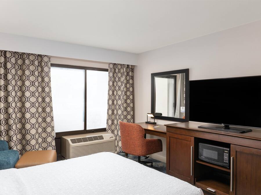 Quarto de hotel com cama, escrivaninha, televisão de tela plana, poltrona e micro-ondas.