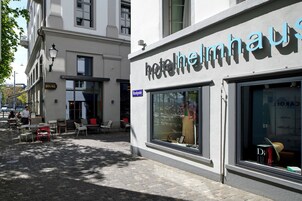 Um hotel chamado 'hotelhelmhaus' com uma grande vitrine, área de estar ao ar livre e rua de paralelepípedos.