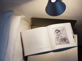 Um livro aberto sobre uma mesa de cabeceira, com uma luminária acima.