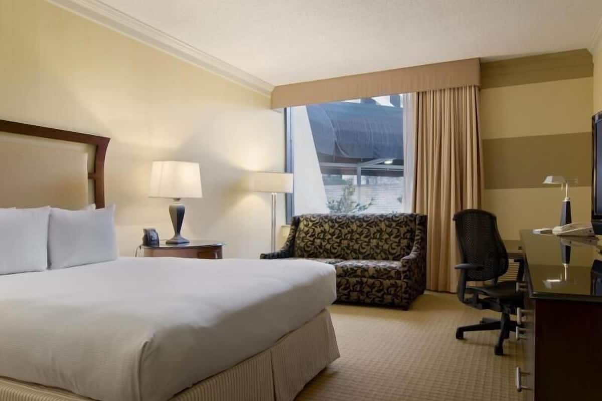 Quarto de hotel com uma cama grande, uma cadeira, uma mesa e vista para o exterior.