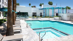 Piscina com espreguiçadeiras e palmeiras, cercada por edifícios modernos.