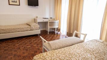 Quarto de hotel com duas camas de solteiro, uma escrivaninha, uma cadeira, uma televisão e janela com cortinas.