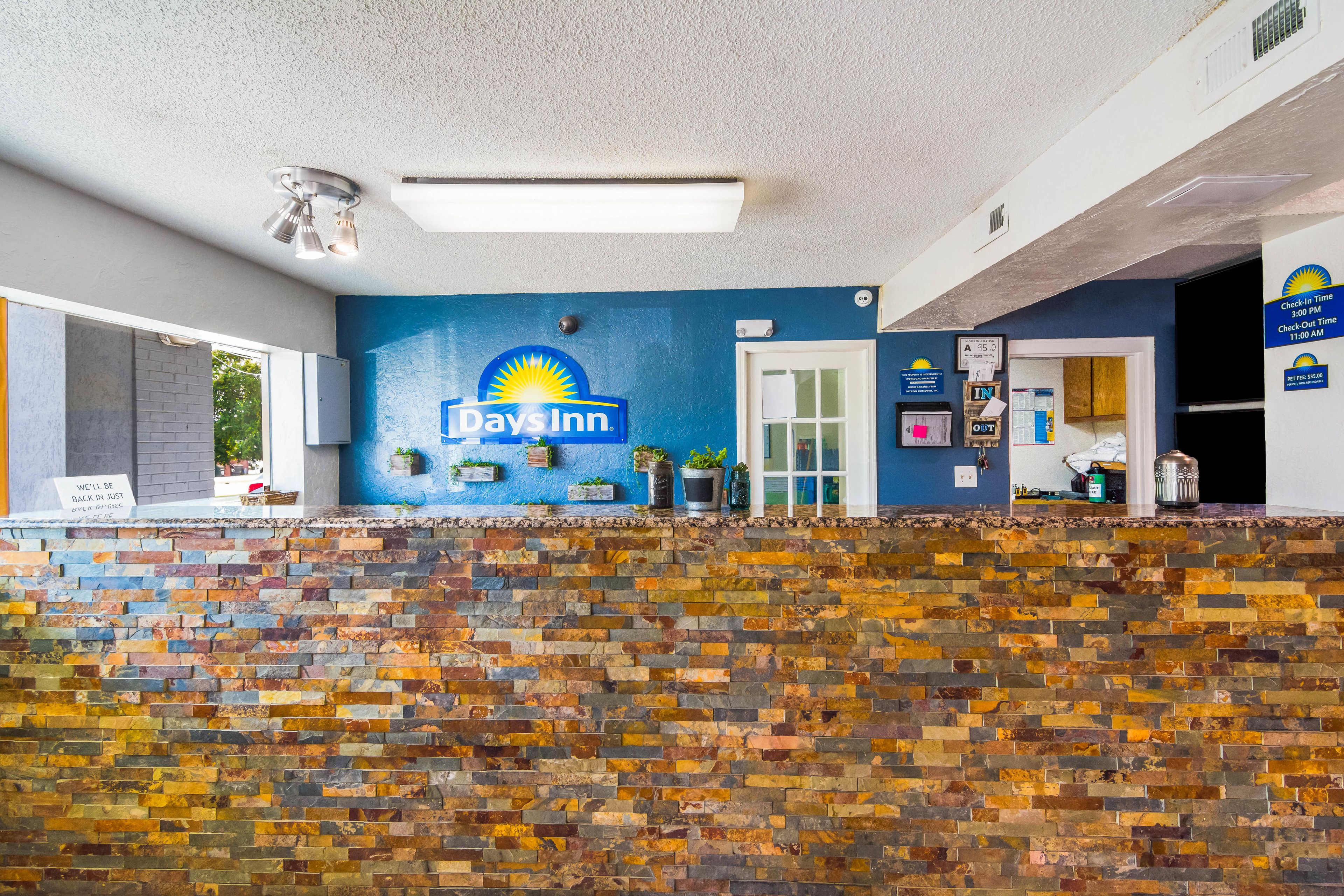 Área de recepção do Days Inn, com parede azul, parede de tijolos e um aviso com os horários de check-in.