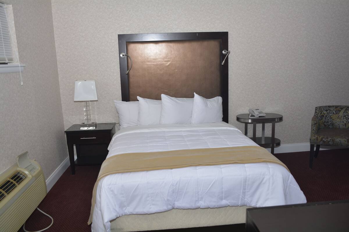 Quarto de hotel com uma cama grande, uma mesa de cabeceira com luminária, uma pequena mesa redonda e uma cadeira.