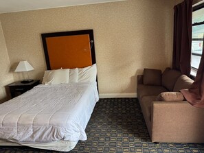 Quarto de hotel com cama, sofá, mesa de cabeceira com luminária e janela com cortinas.