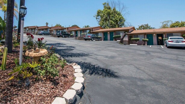 Fileira de edifícios de motel com parque de estacionamento pavimentado e jardim ajardinado com cactos e arbustos.