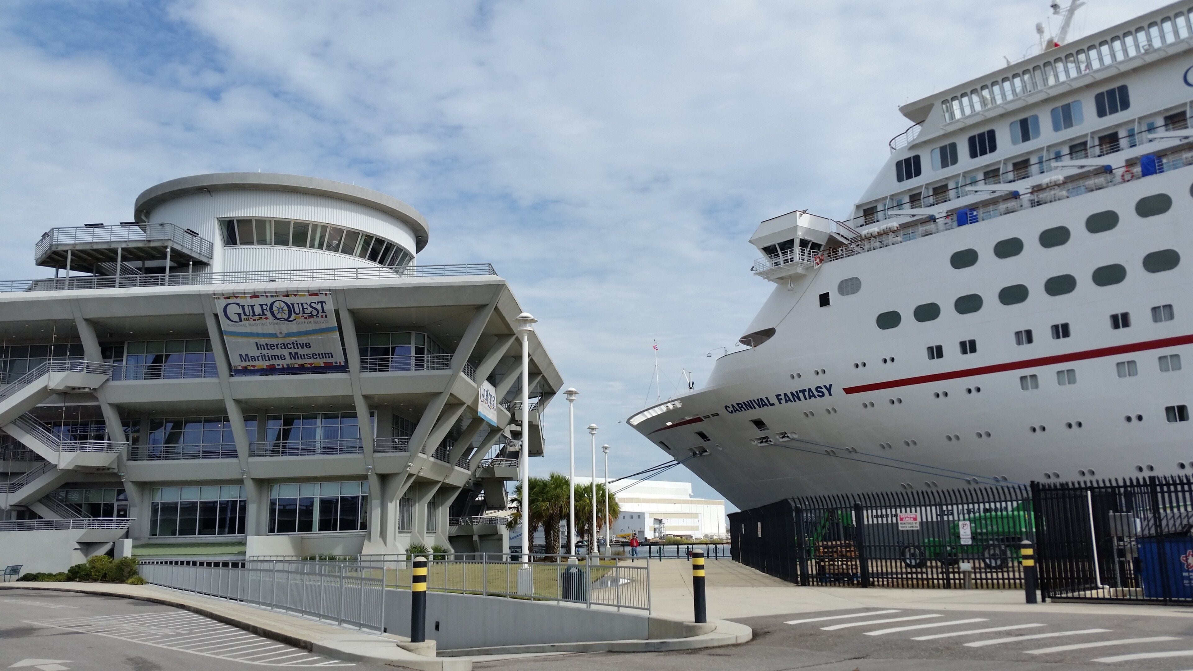 Um cruzeiro atracado em um porto, com um edifício ao fundo identificado como 'GulfQuest Interactive Maritime Museum'.