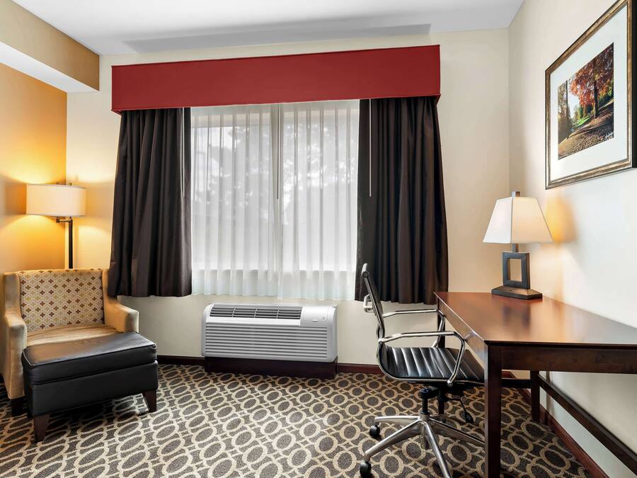 Quarto de hotel com carpete estampado, uma escrivaninha, uma cadeira, um sofá e uma janela com cortinas.